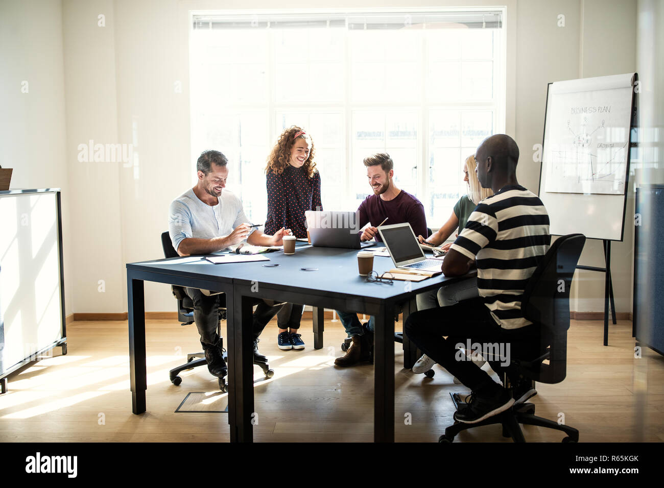 Diverse group of young designers discussing work together while sitting ...