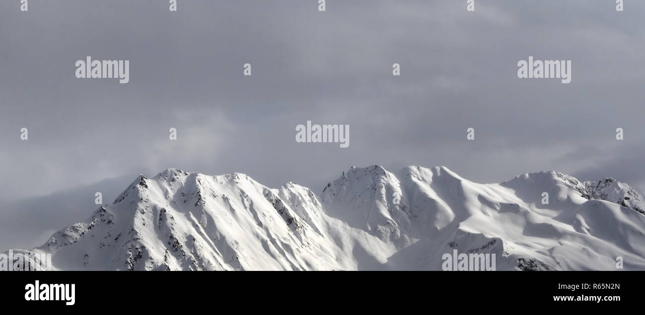 Panoramic view on evening snowy sunlight mountains and gray sky ...