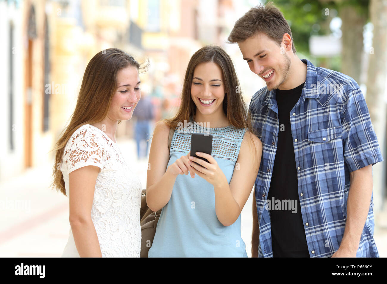 Three happy friends checking smart phone content standing in a street ...