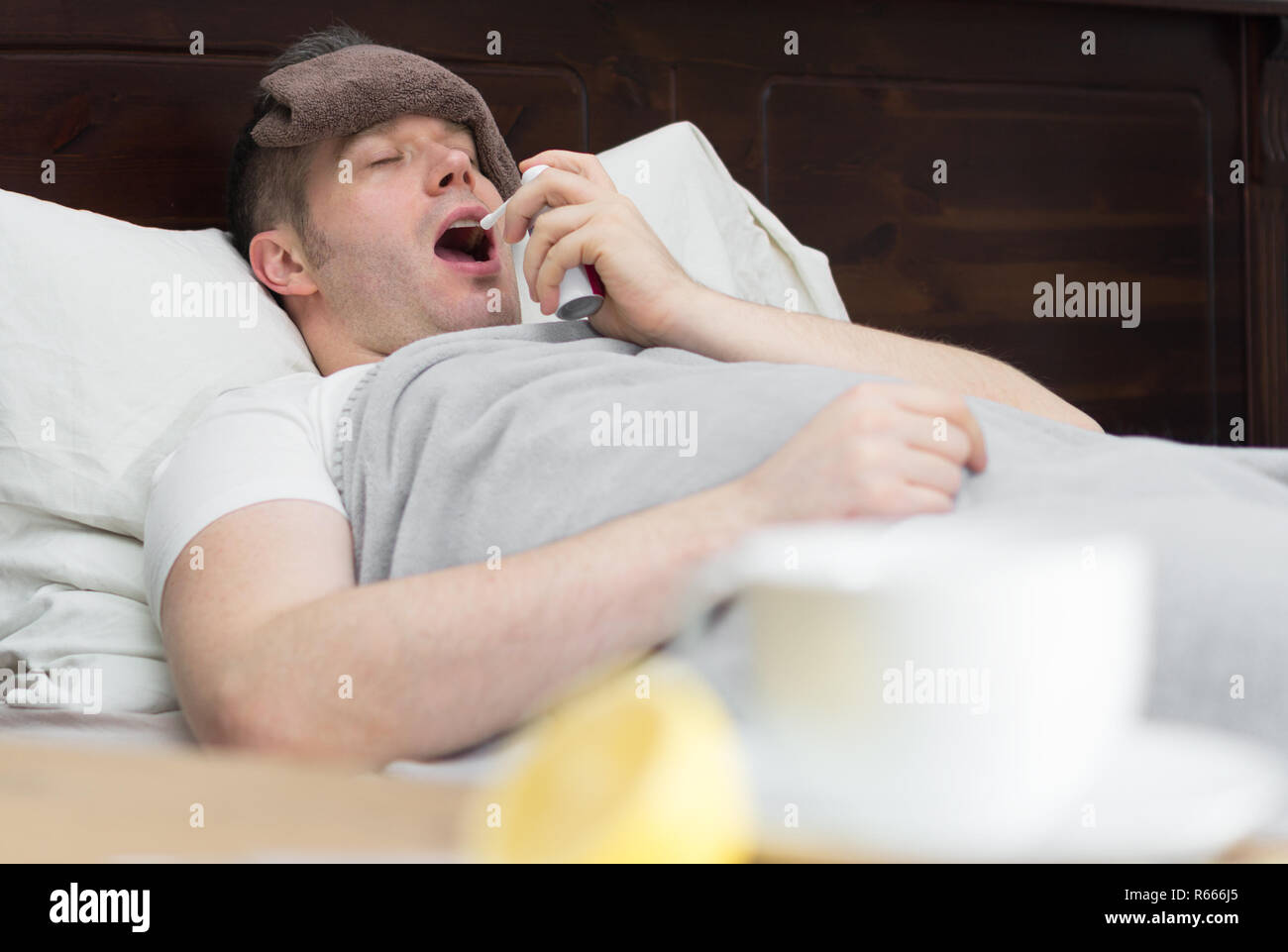 Sick man using mouth spray in the bed Stock Photo - Alamy