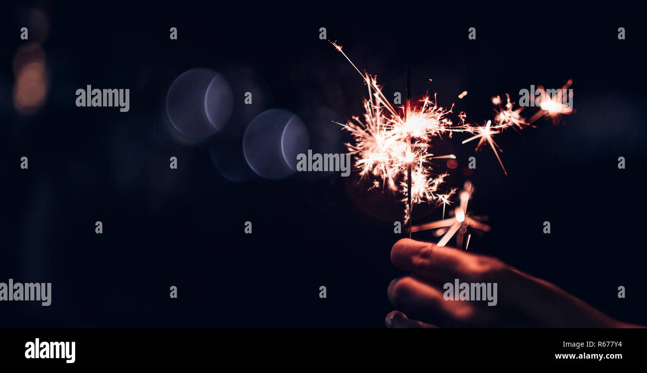 Hand holding burning Sparkler blast on a black bokeh background at ...