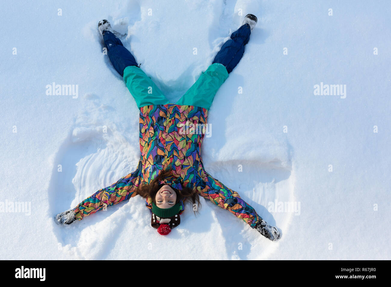 High angle view of happy girl lying on snow and moving her arms and ...