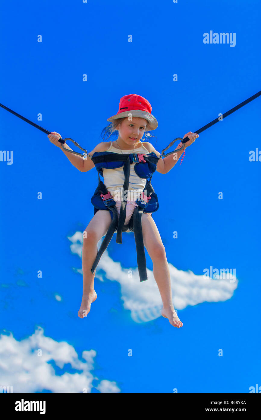 Children jumping on a trampoline with rubber ropes against the blue sky ...