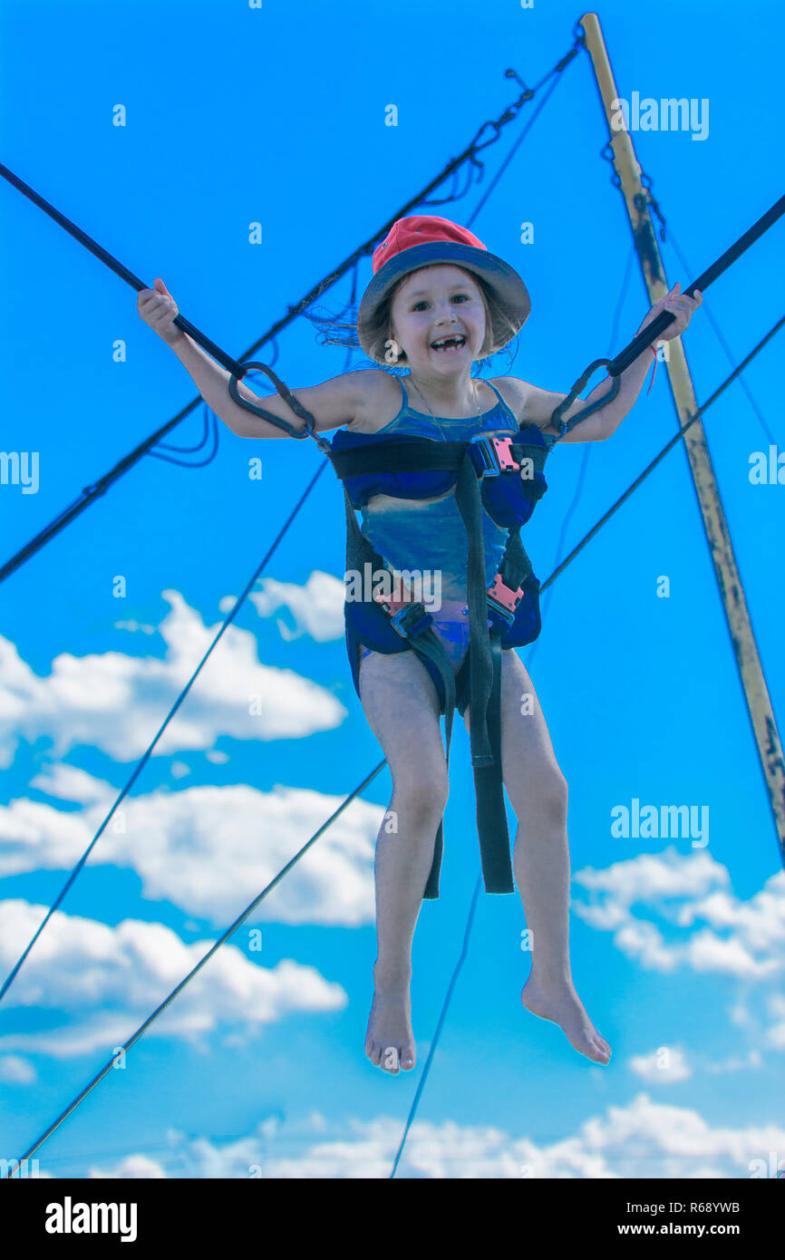 Children jumping on a trampoline with rubber ropes against the blue sky ...
