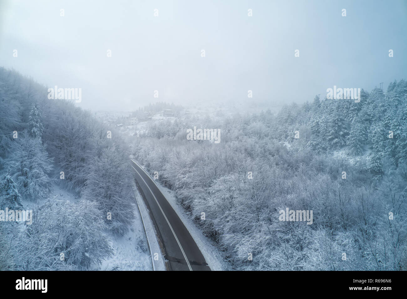 Aerial view of snowy forest with a road in the area of Vermio in ...