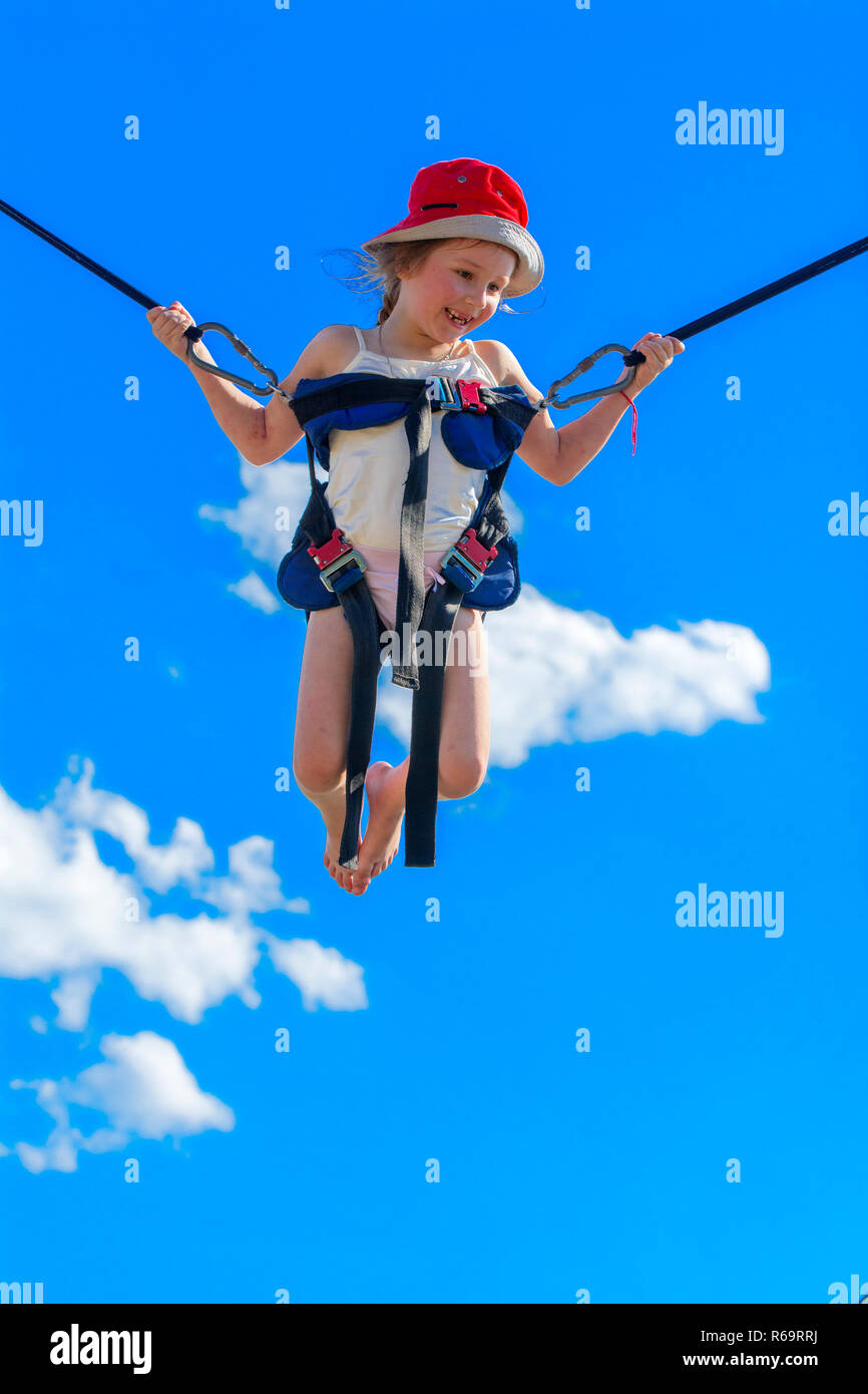 Children jumping on a trampoline with rubber ropes against the blue sky ...