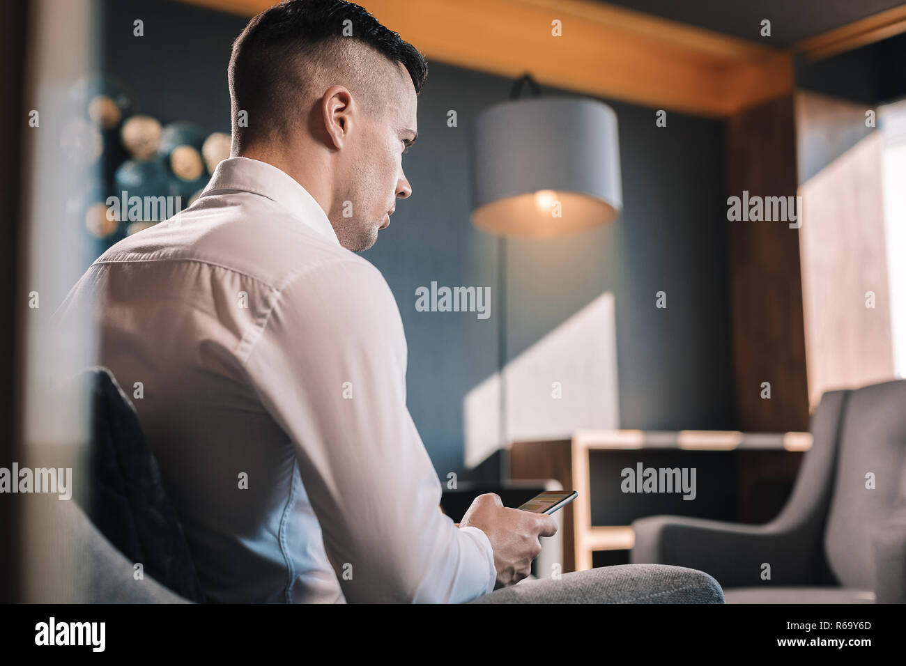 Young but prosperous businessman sitting in his office using phone ...