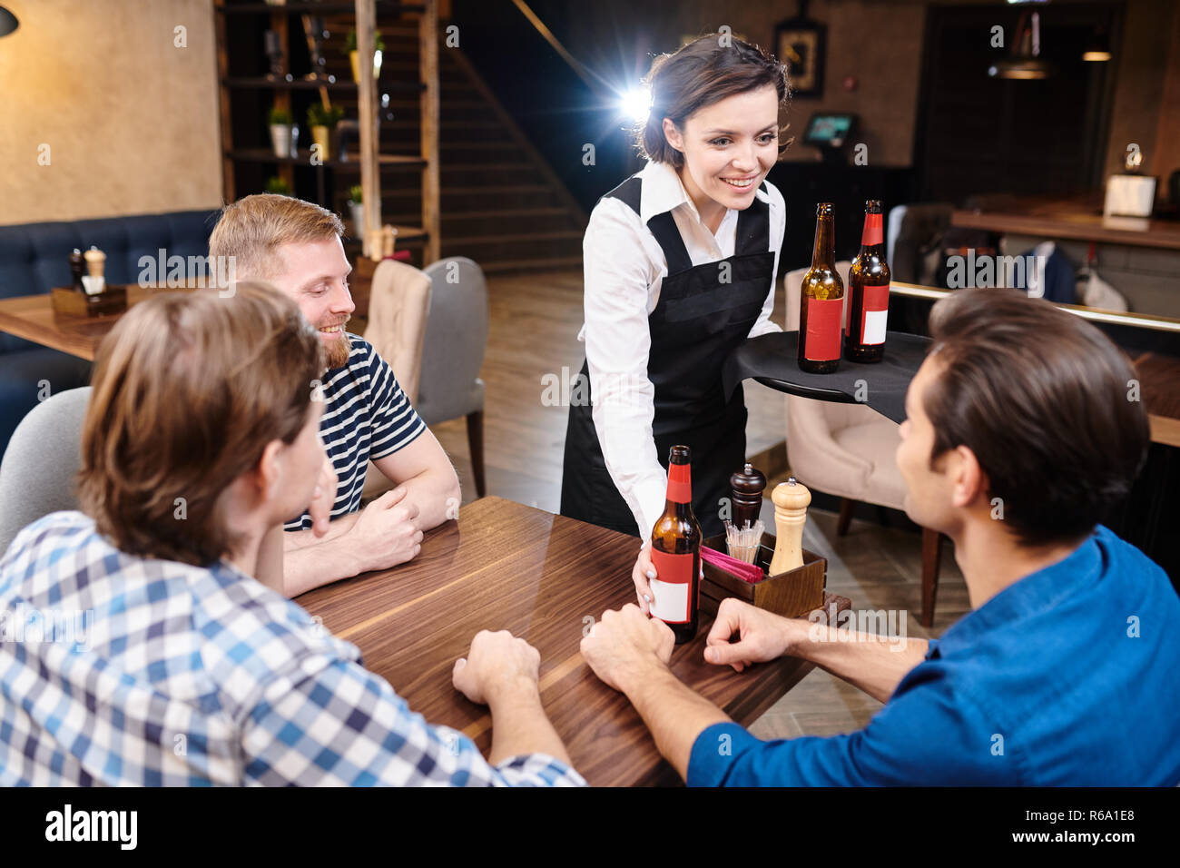 Smiling content beautiful young lady waitress in black apron giving ...