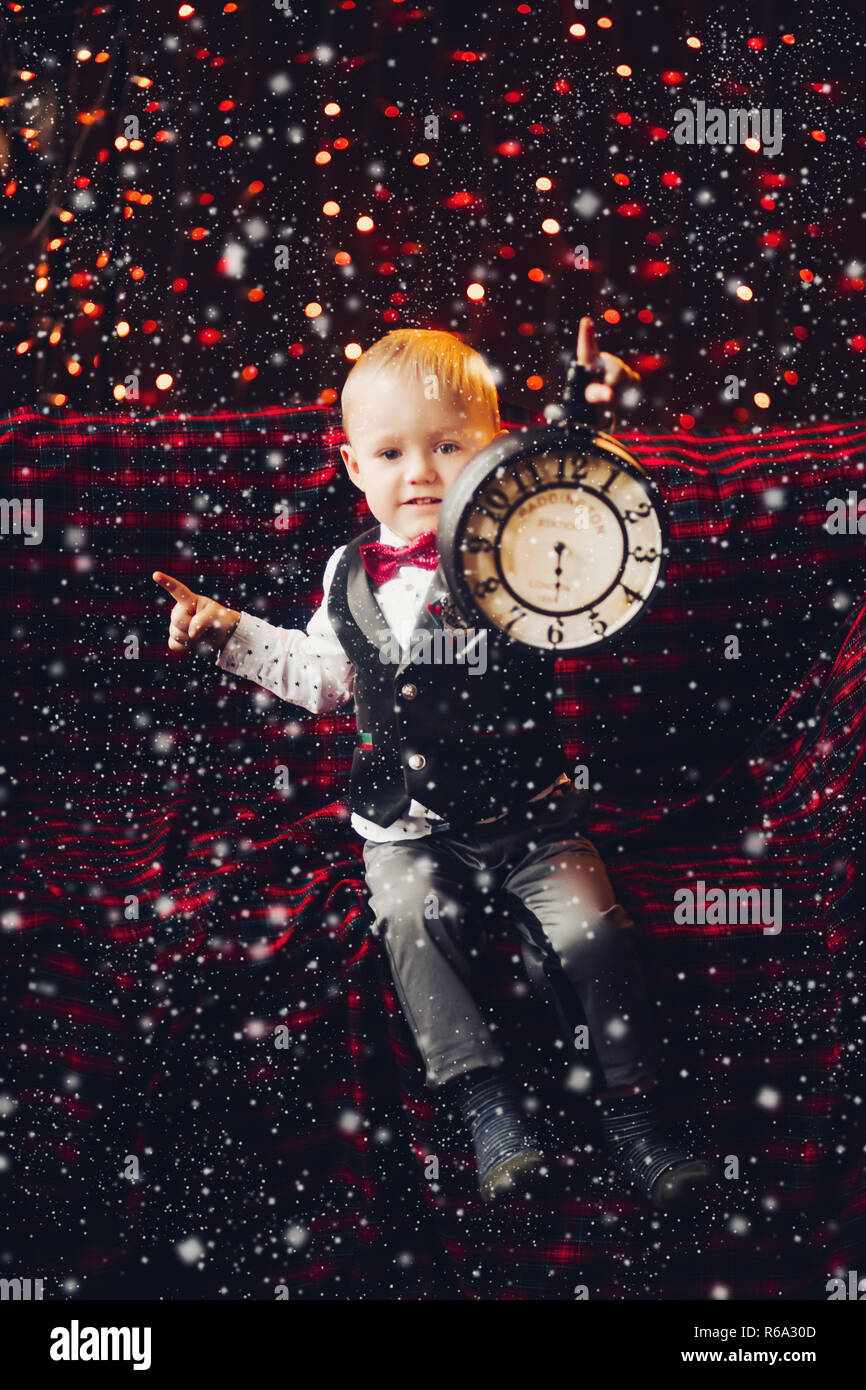 Handsome and cute little boy posing in studio and showing big clock ...