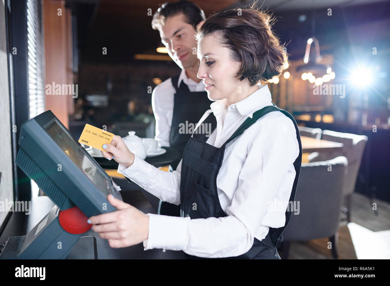 Content attractive young waitress with short hair swiping card through ...