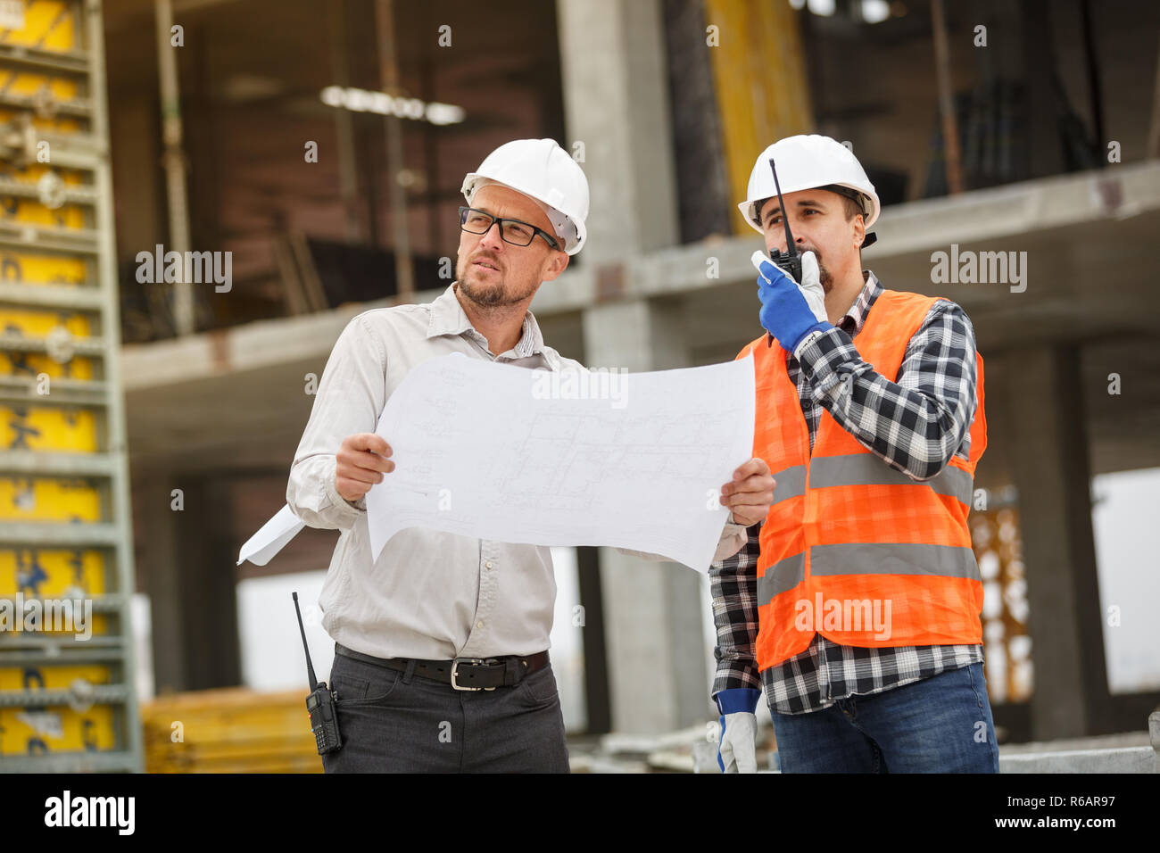Male architect and developer with walkie talkie discussing blueprints ...