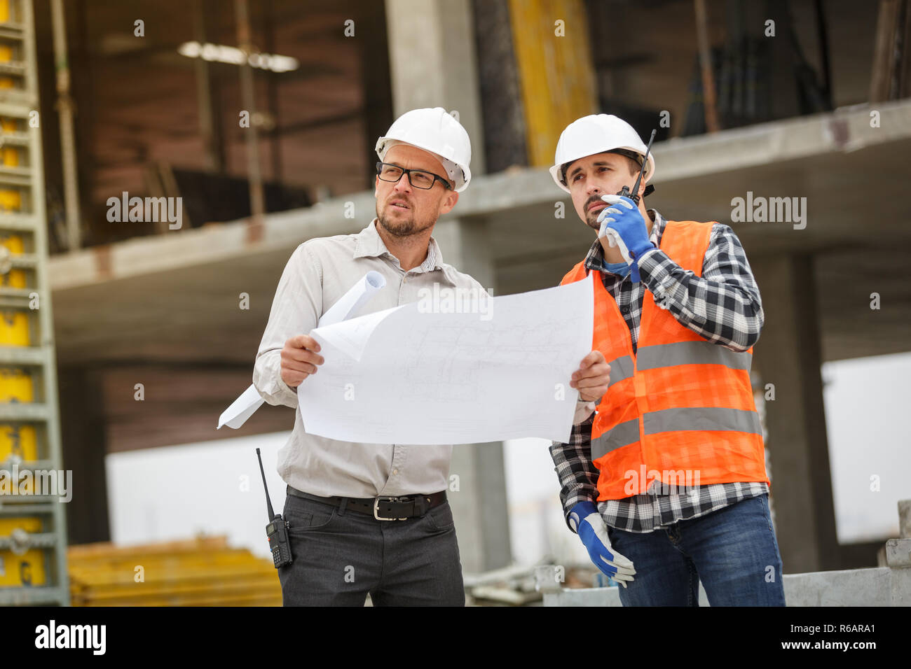 Male architect and developer with walkie talkie discussing blueprints ...