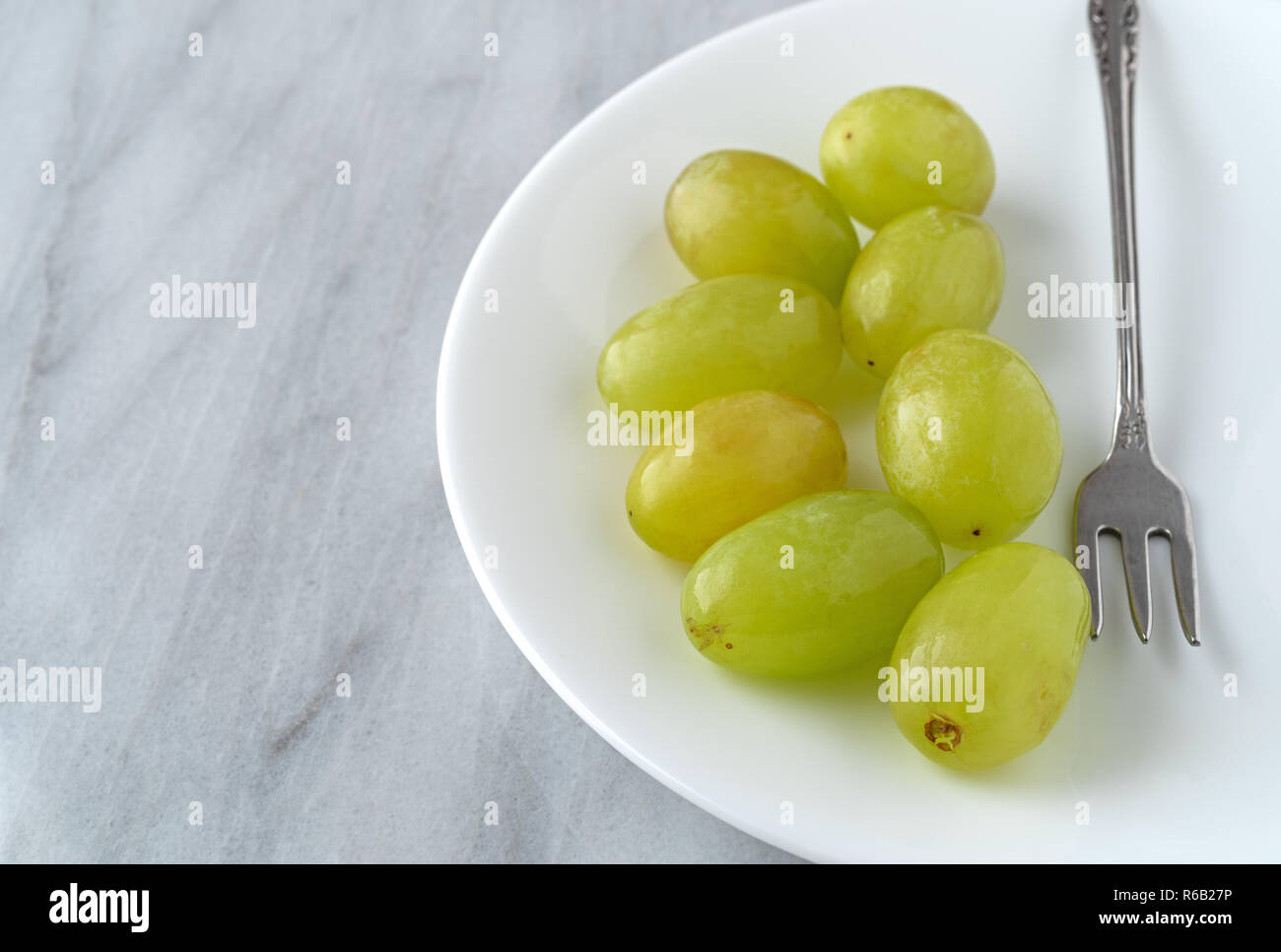 Side view of a serving of green grapes with a fork to the side on a ...