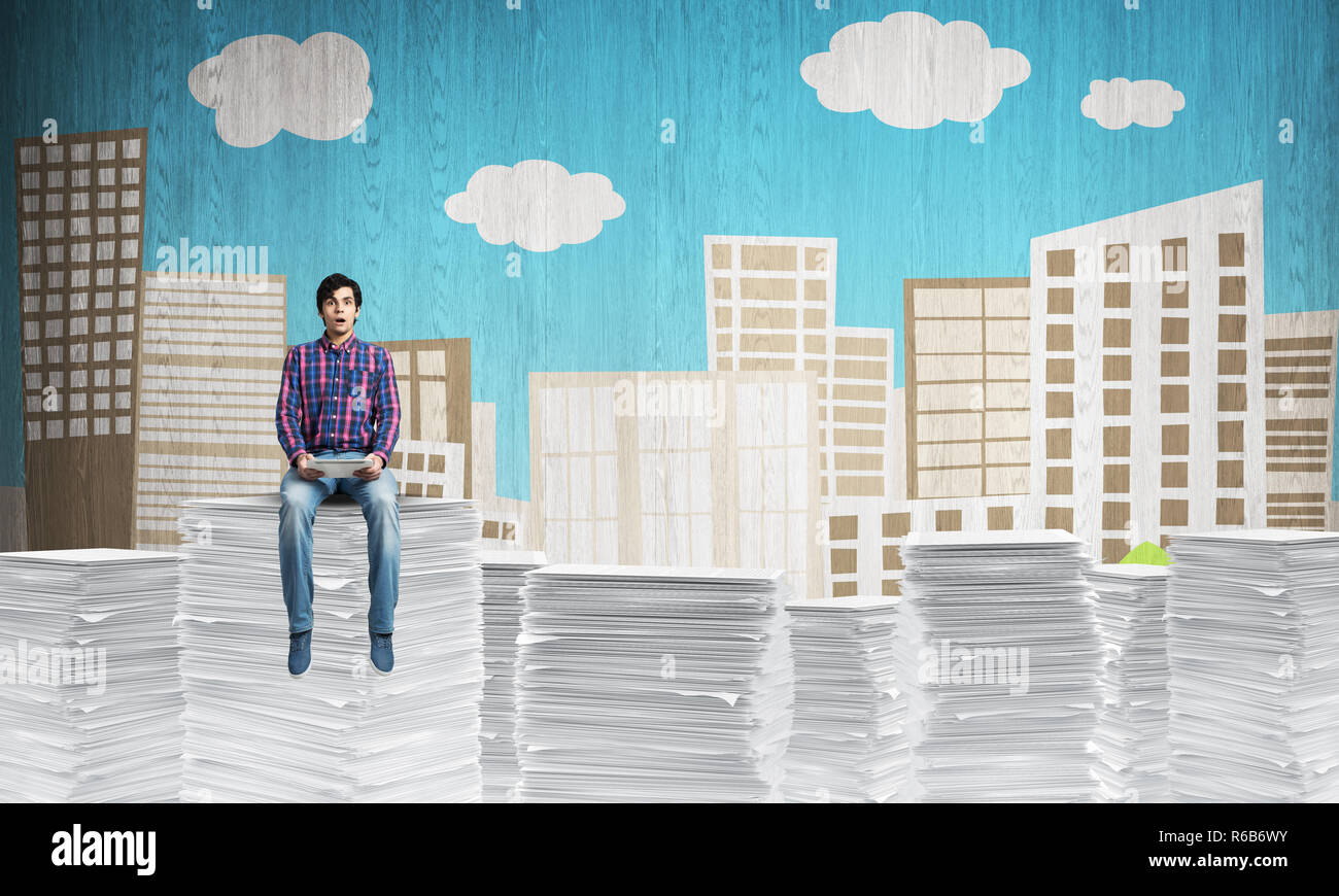 Young man sitting on pile of paper documents Stock Photo - Alamy