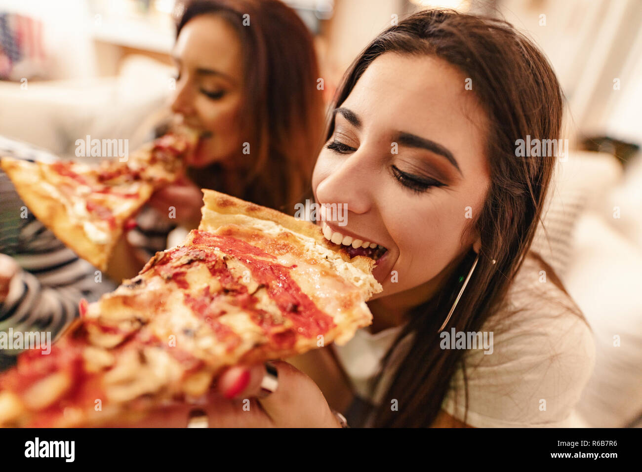 Excited young women are eating pizza sitting on sofa. They have great ...