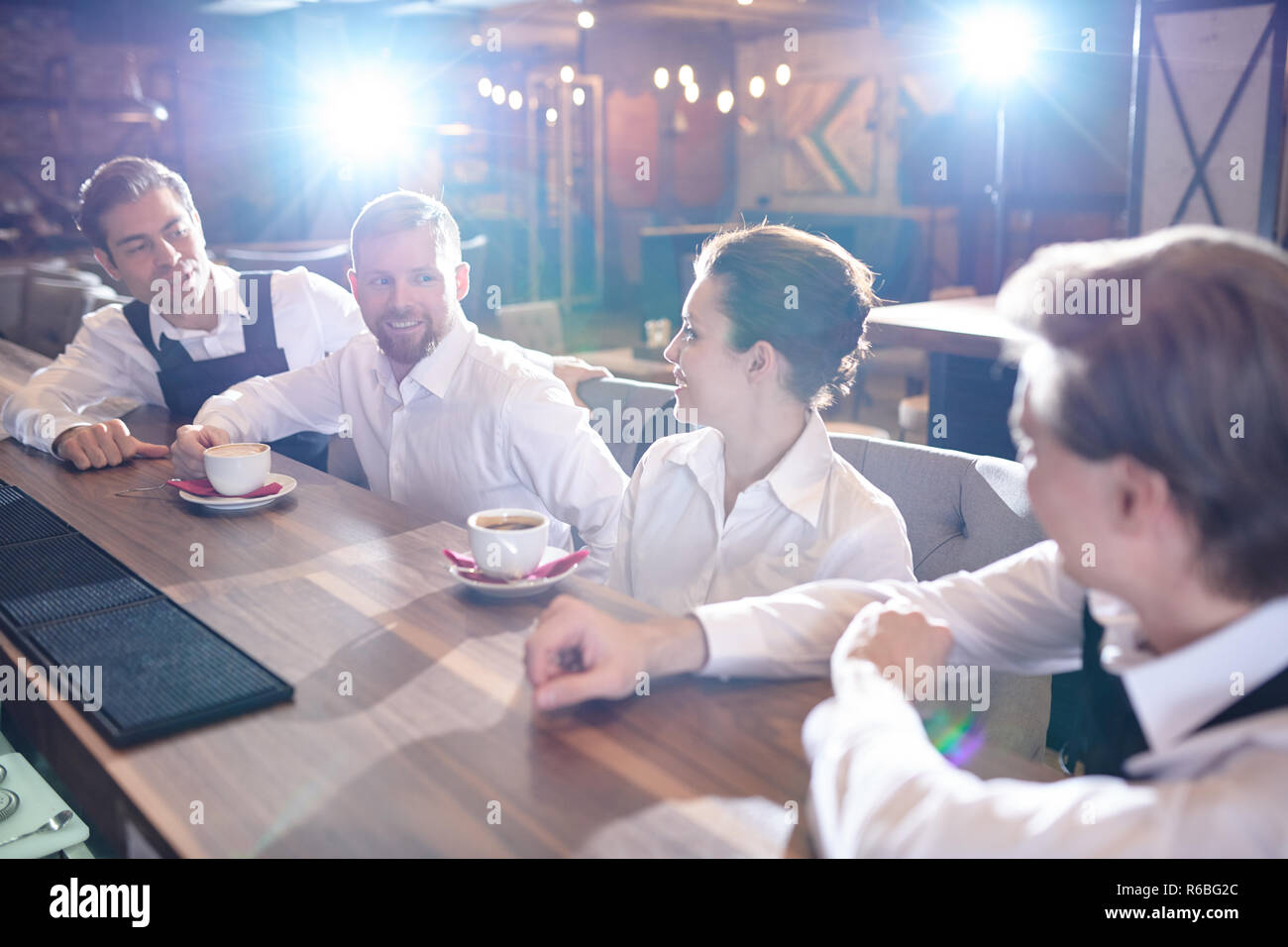 Cheerful excited restaurant staff in white shirts sitting at bar ...