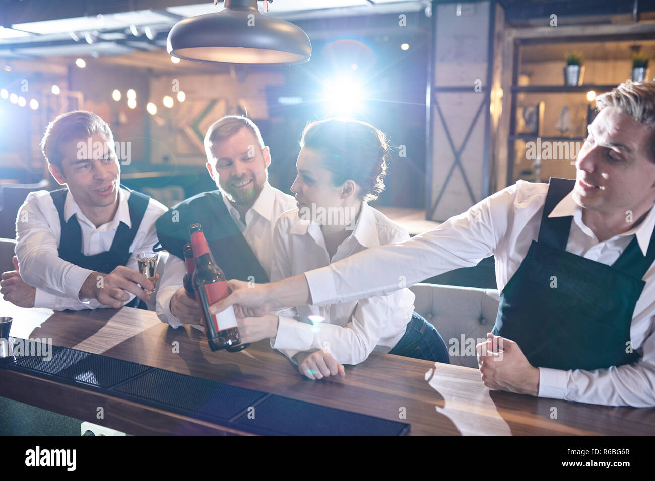Group of positive happy waiters in uniform leaning on bar counter and ...