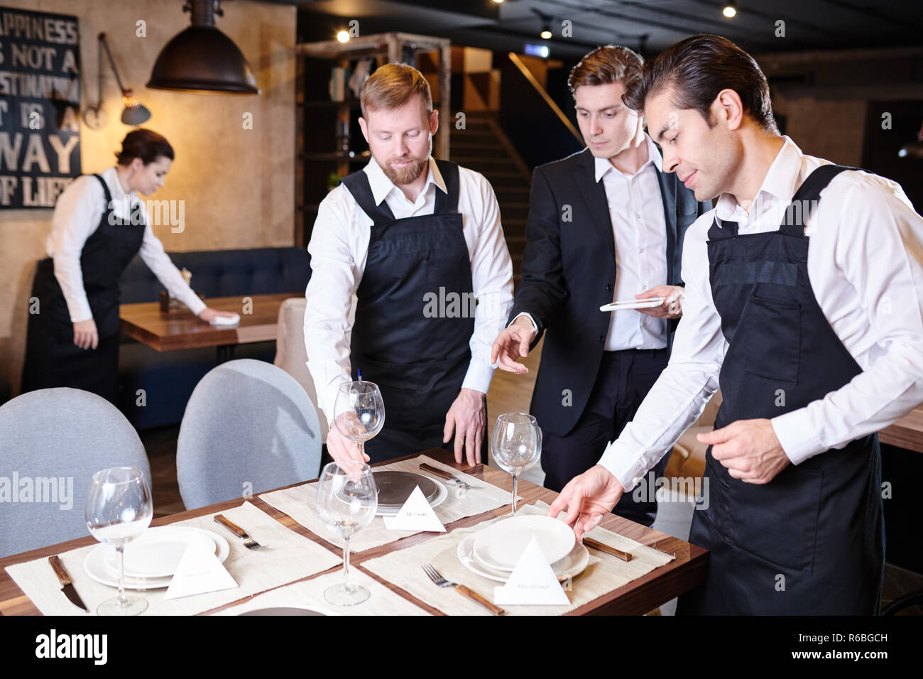 Serious restaurant manager in formal suit standing at table and ...