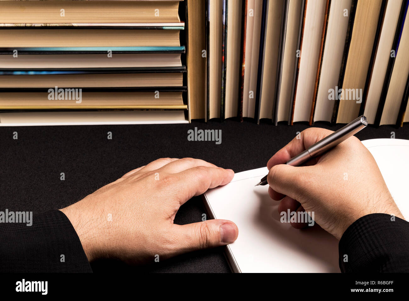 the hand of a man writing in a blank book beside a book background ...