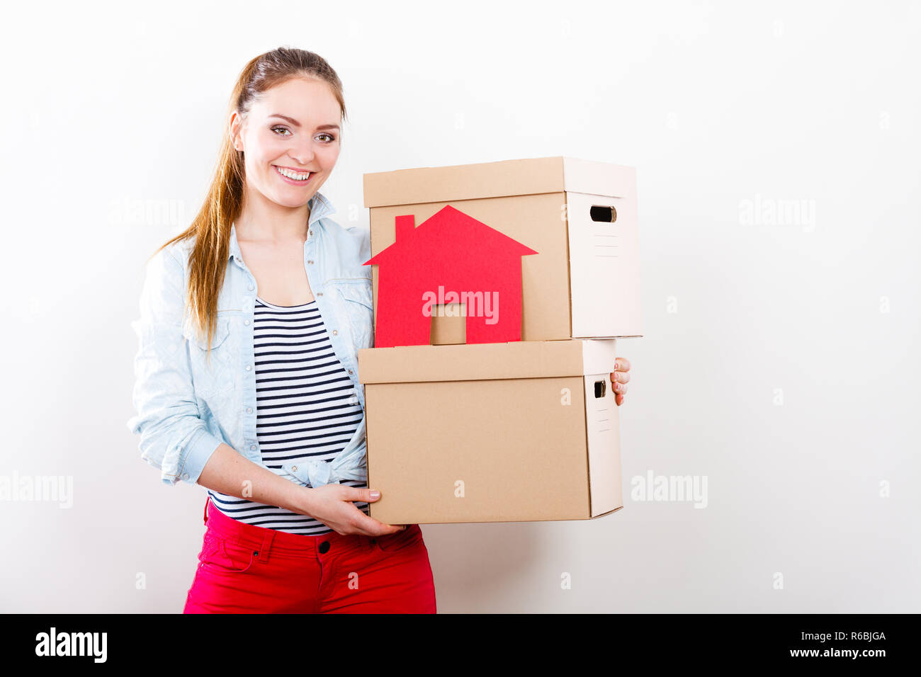 Happy woman moving into new apartment carrying cartons boxes with red ...