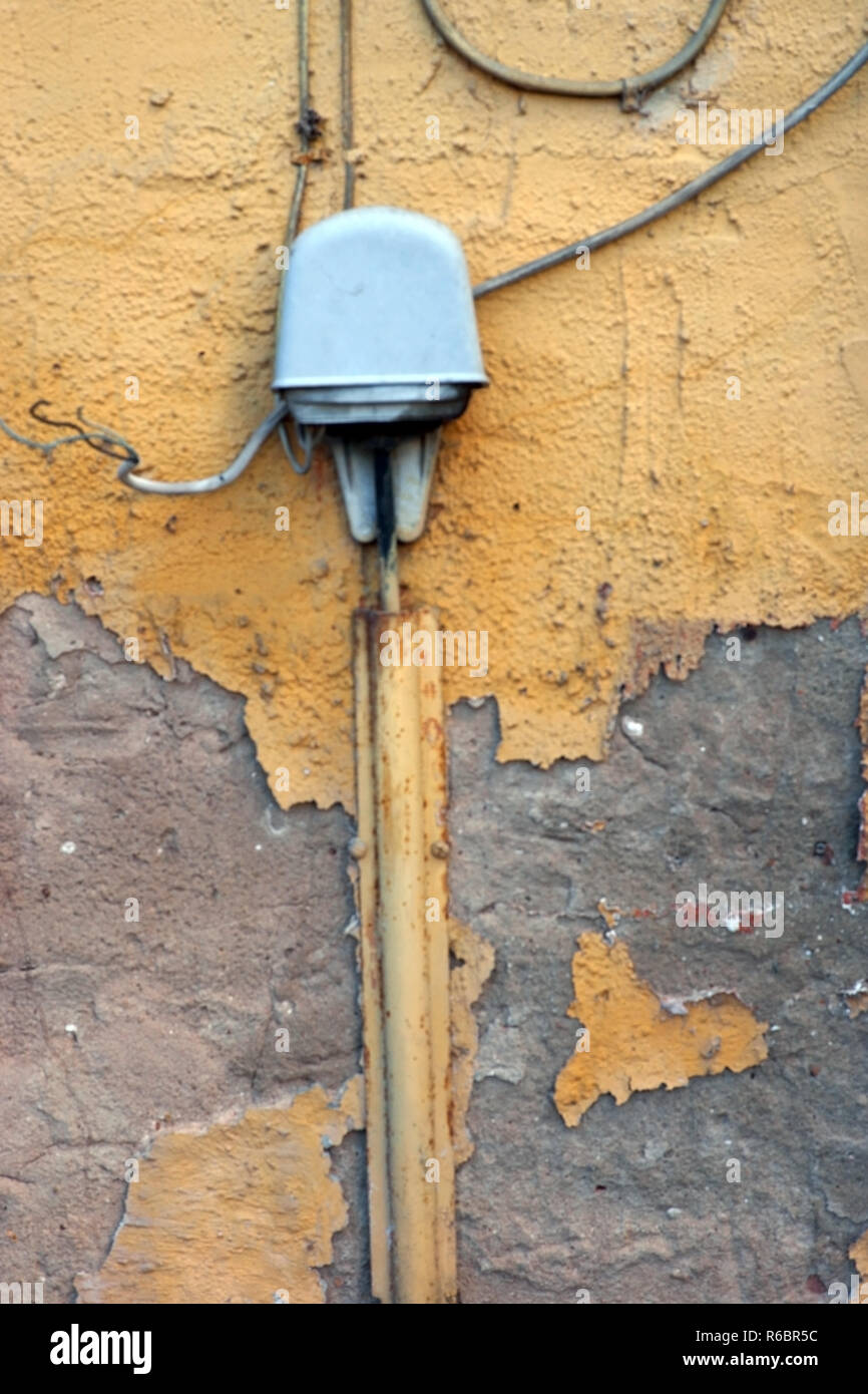 A staid and old power distribution box with torn off cables on a wall ...