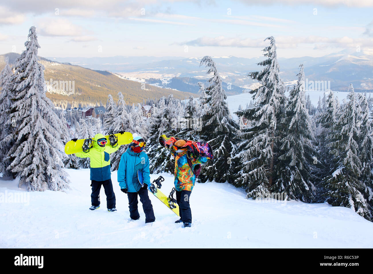 Three snowboarders walking at ski resort. Friends climbing to mountain ...