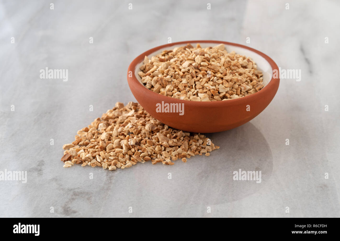 Side view of a small bowl of cut orris root with spilled herb to the ...