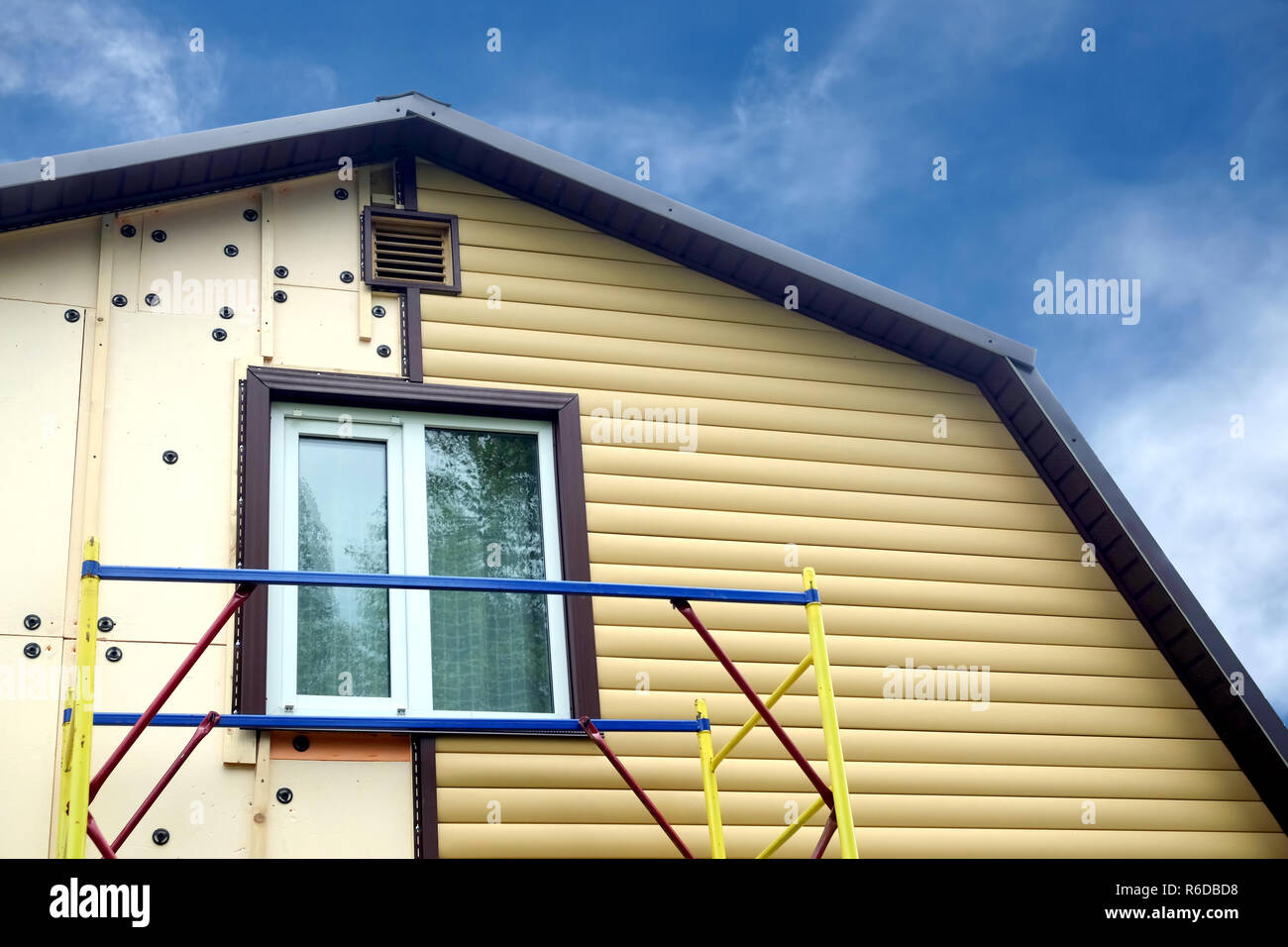 Beige siding panels mounting with scaffolding on beautiful rural house ...