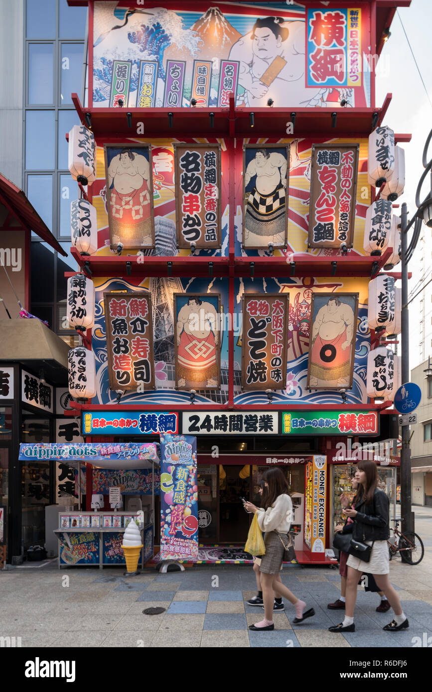 Japanese girls walk by a building full of signs in the Shinsekai ...