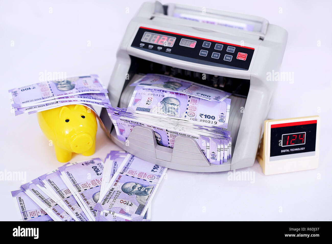 Money counting machine with new 100 rupees notes and yellow piggy bank ...