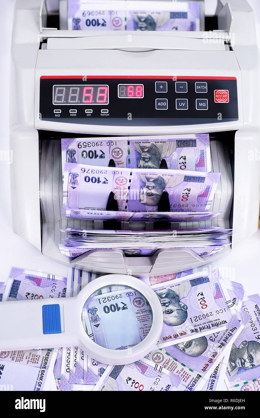 Money counting machine with new 100 rupees notes and magnifying glass ...