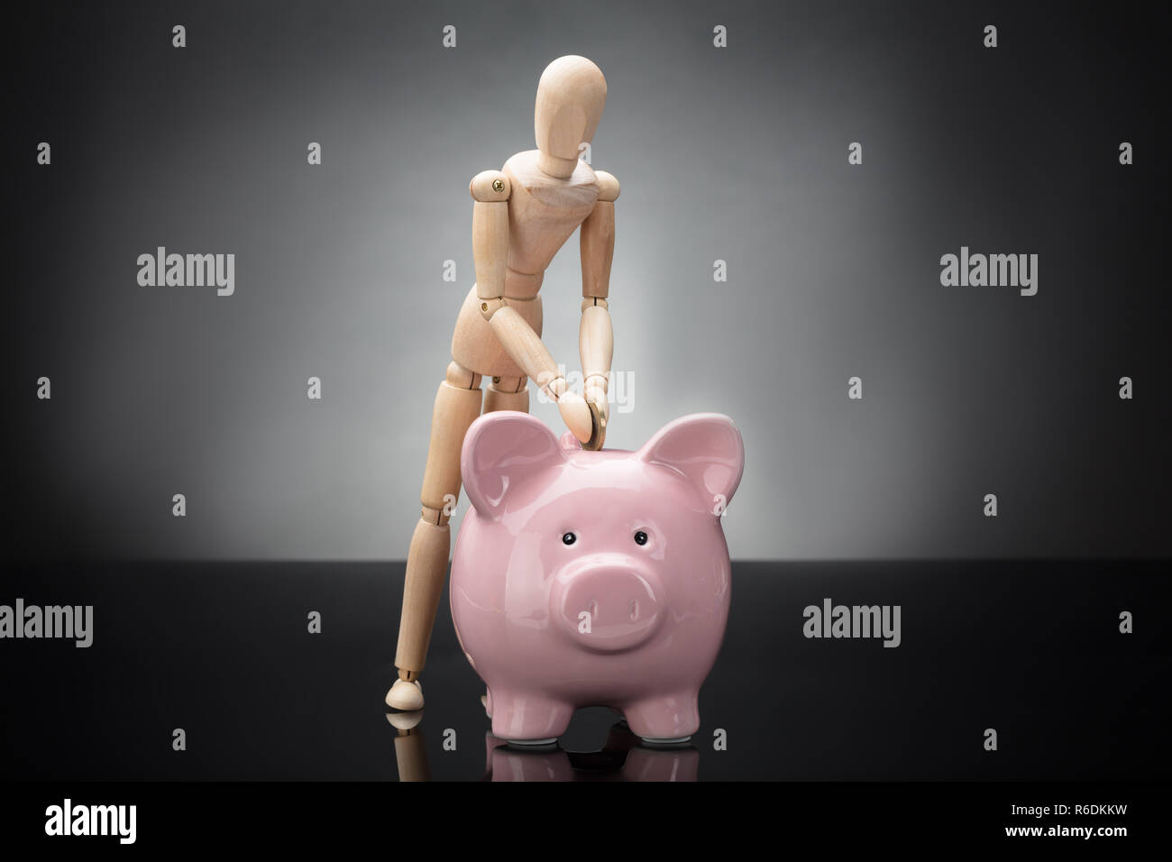 Wooden Dummy Inserting Coin In Piggy Bank Stock Photo - Alamy