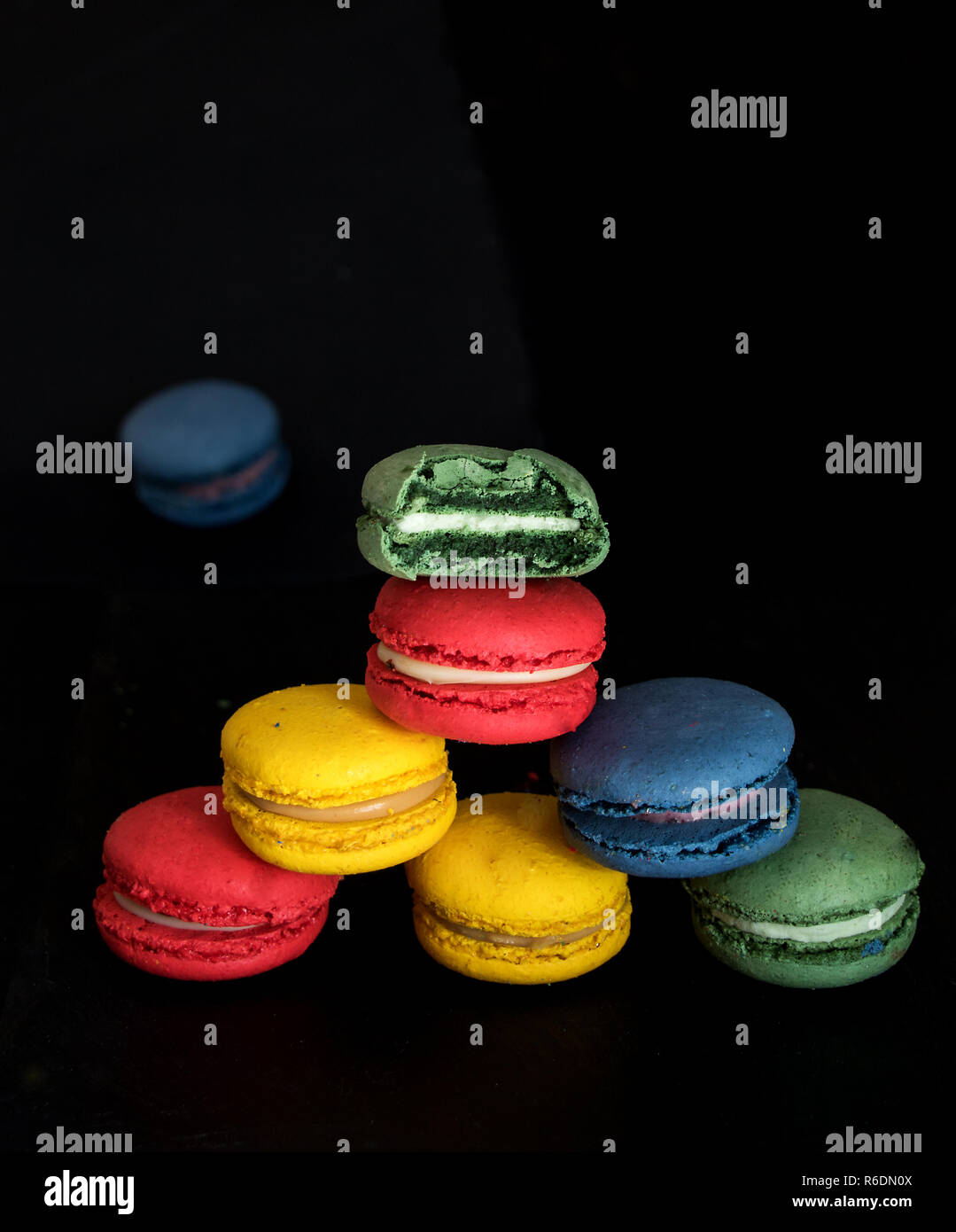 colorful macaroons and a bitten part stacked in front of black ...