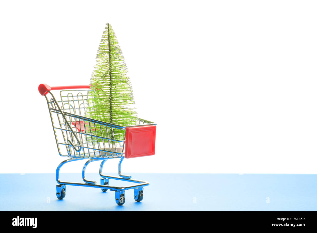 Small artificial fir tree into shopping cart on blue and white ...