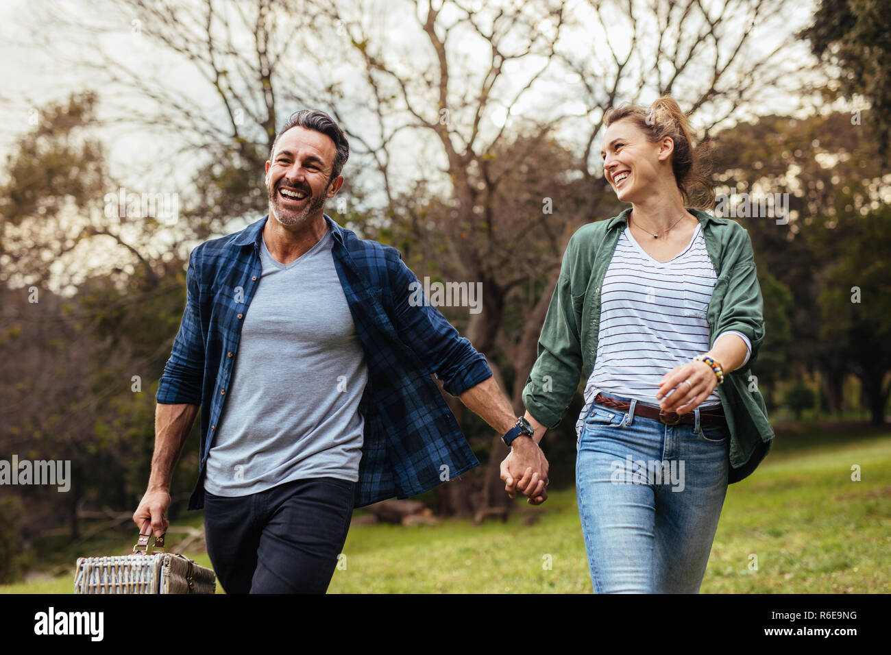 Happy Couple Walking In The Park Holding Hand And Carrying Picnic