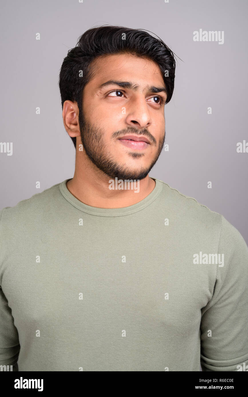 Portrait of young handsome Indian man thinking against gray background ...