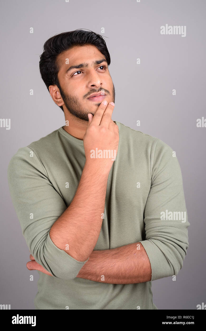 Portrait of young handsome Indian man thinking against gray background ...