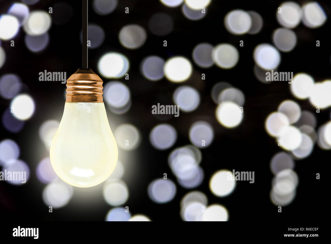 Illuminating light bulb hanging with colorful blurred Christmas lights ...