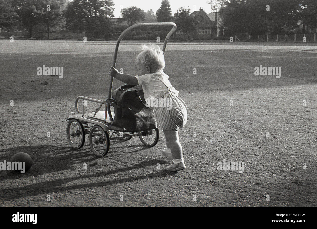 1950s, historical, an infant child pushing a pushchair on a cricket ...