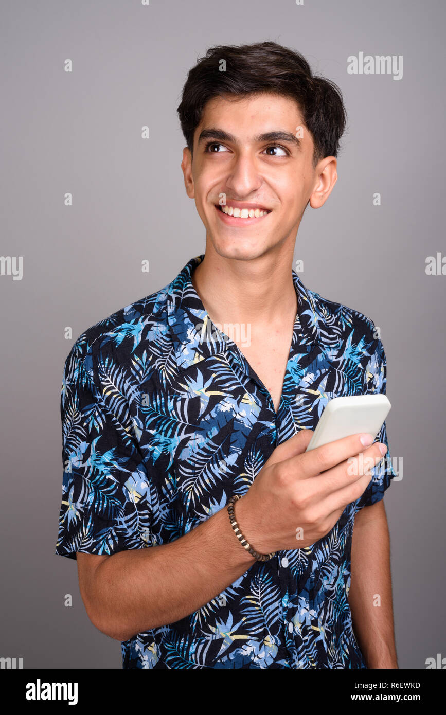 Happy young Persian teenage boy thinking and using mobile phone Stock ...