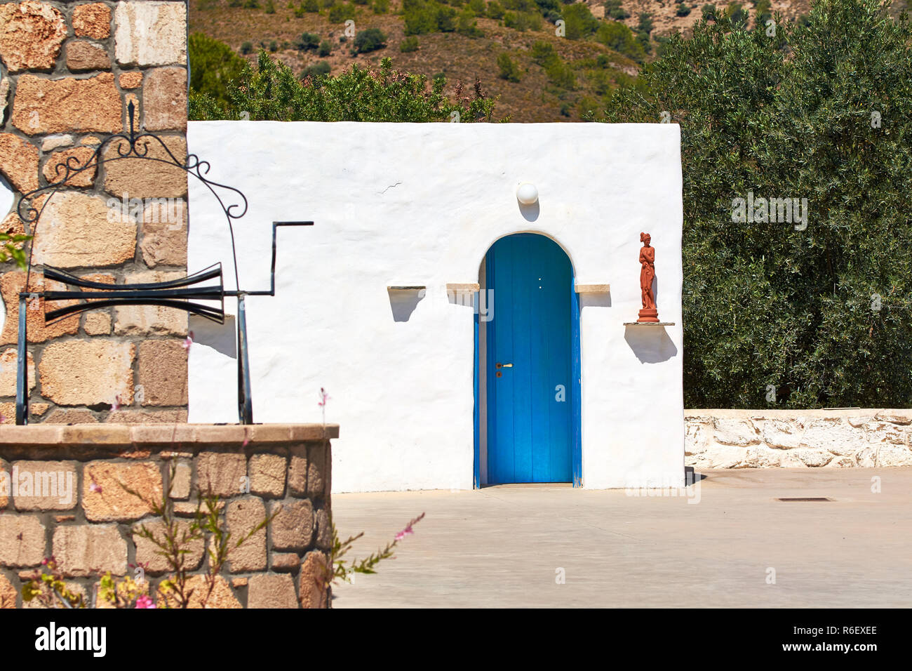 White clay Greek house with a blue door, a stone well and a statue at ...