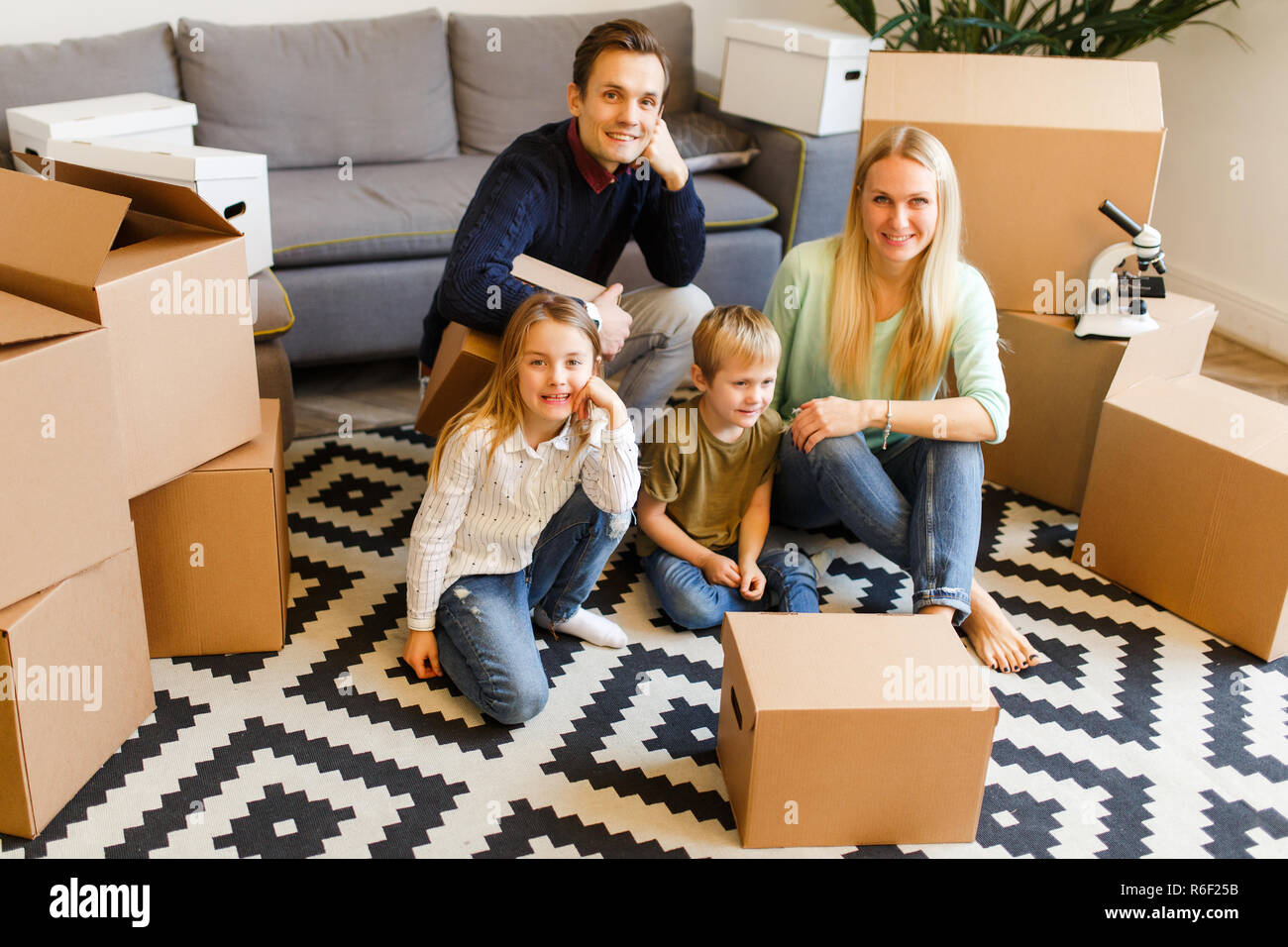 Photo of parents with children sitting on floor among cardboard boxes t ...