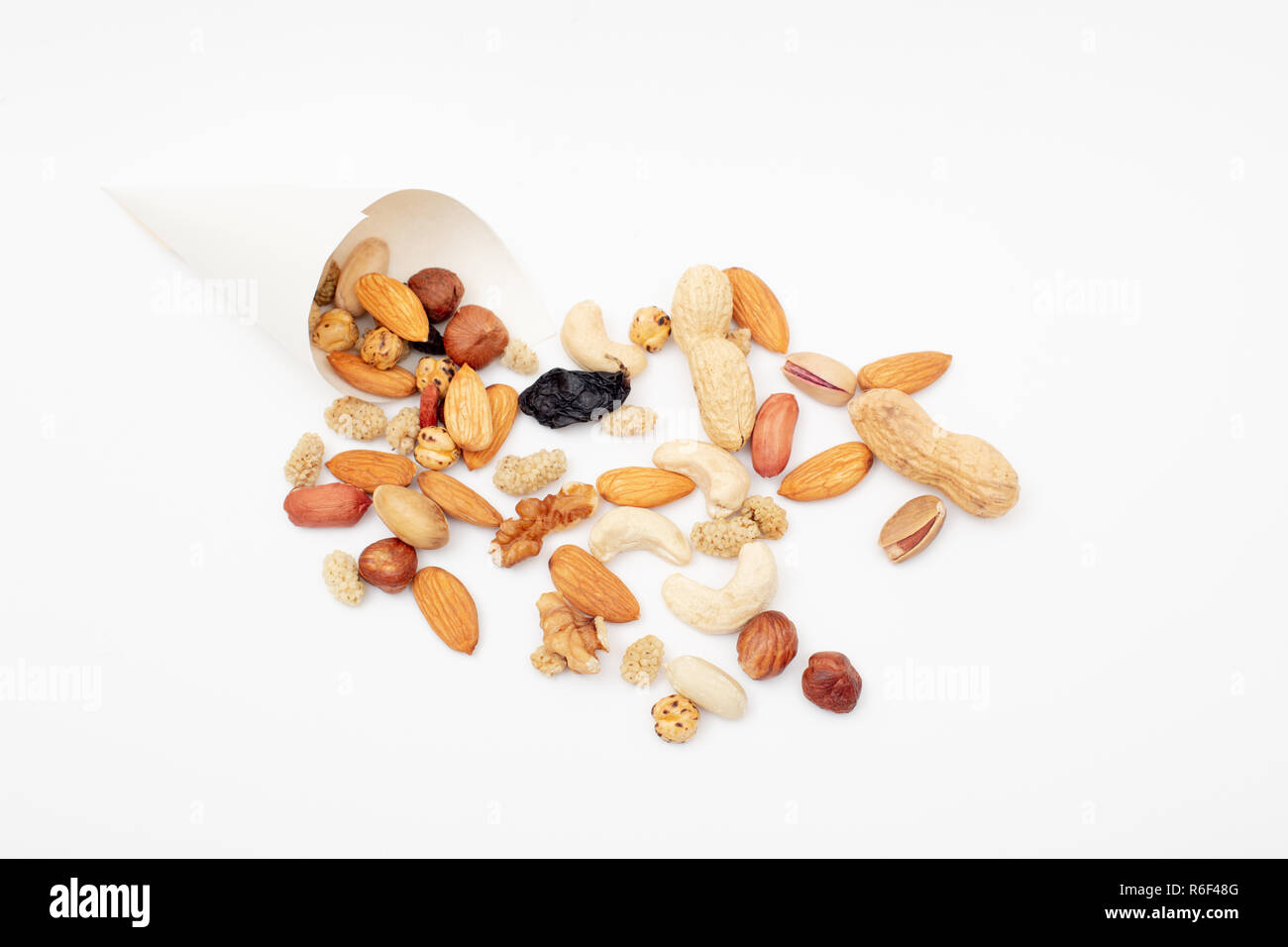 Assorted Nuts spill out of a paper cone on white background close up ...