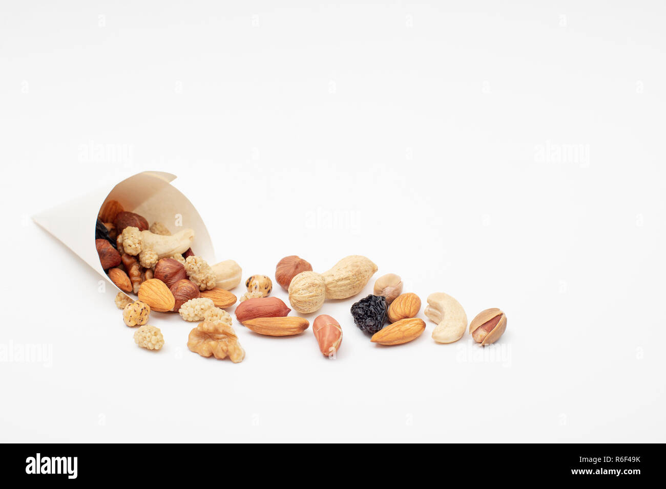 Assorted Nuts spill out of a paper cone on white background close up ...