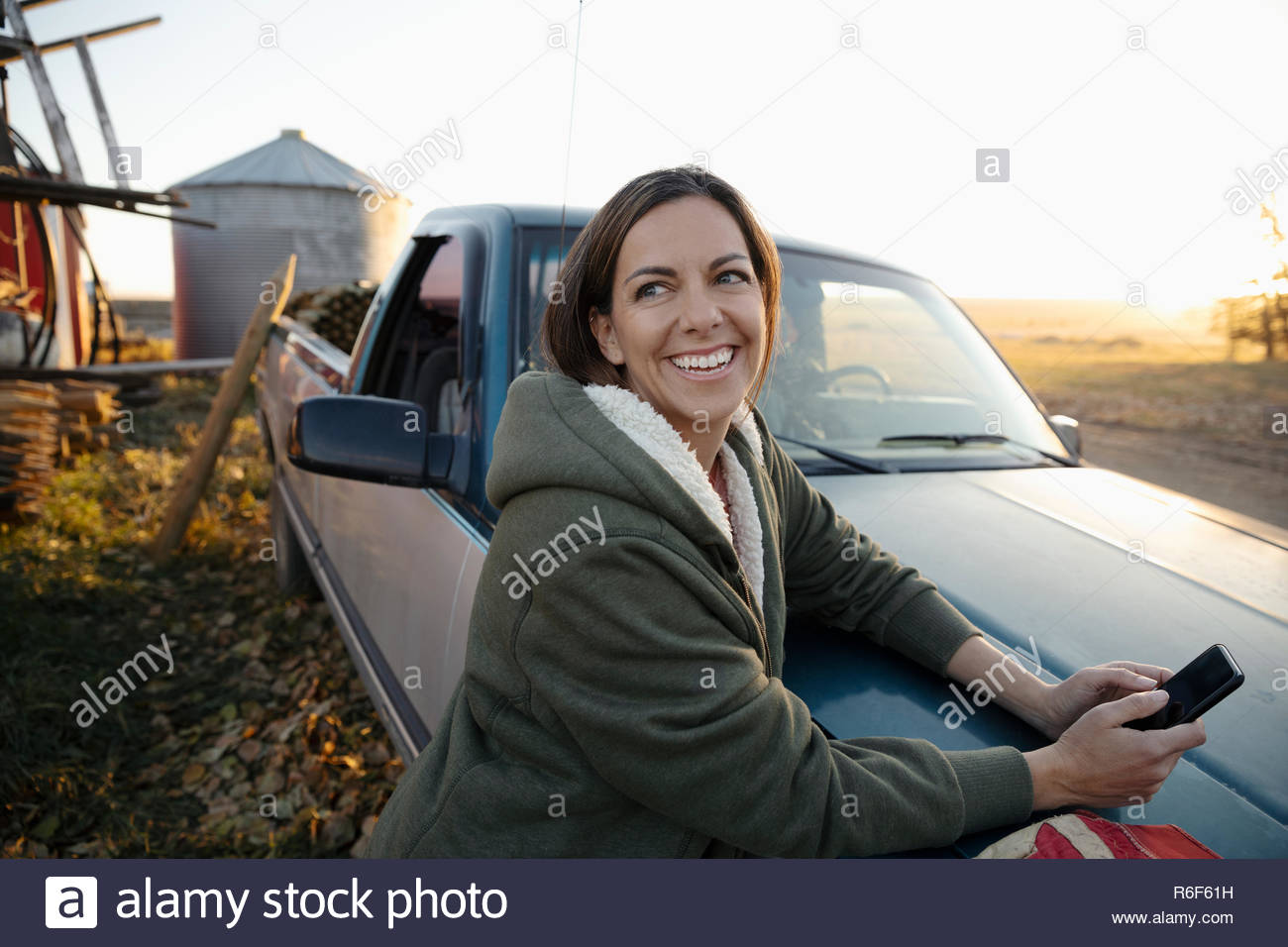 Smiling, happy female farmer using smart phone at pickup truck on farm ...