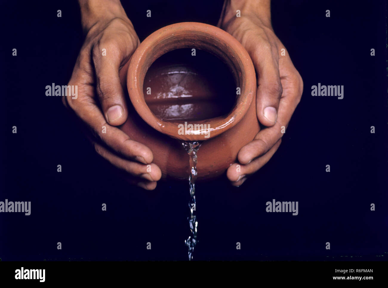 man hands holding earthen pot and pouring water on black background ...