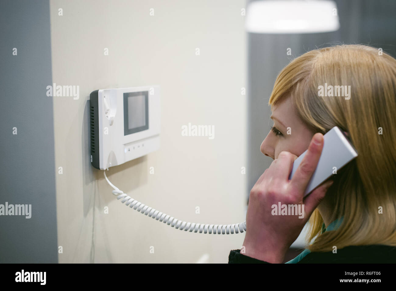 blonde woman answers the intercom call while holding the phone to your ...