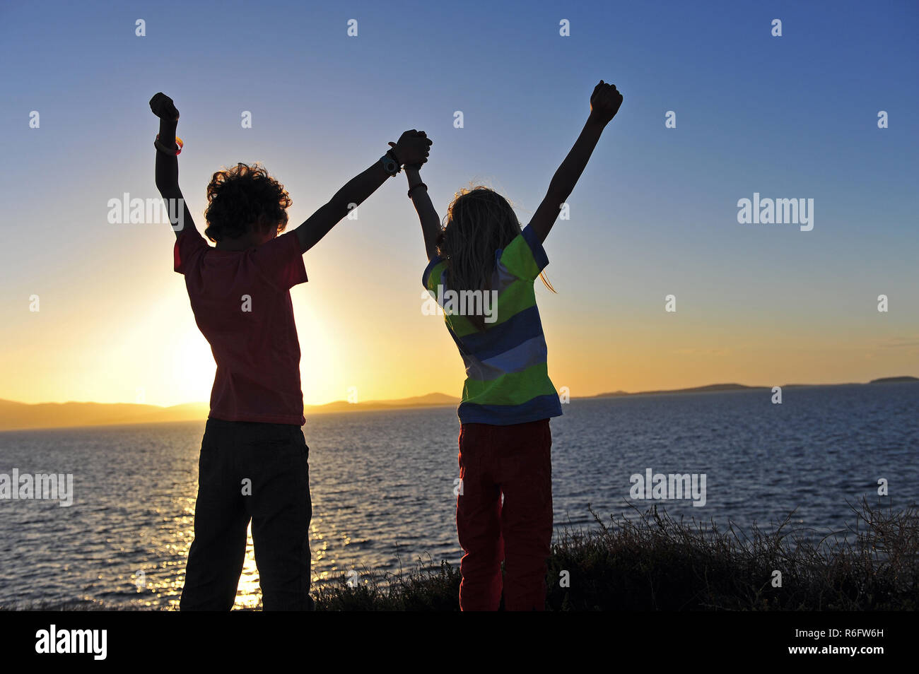 Two kids with hands in the air on sunset Stock Photo - Alamy