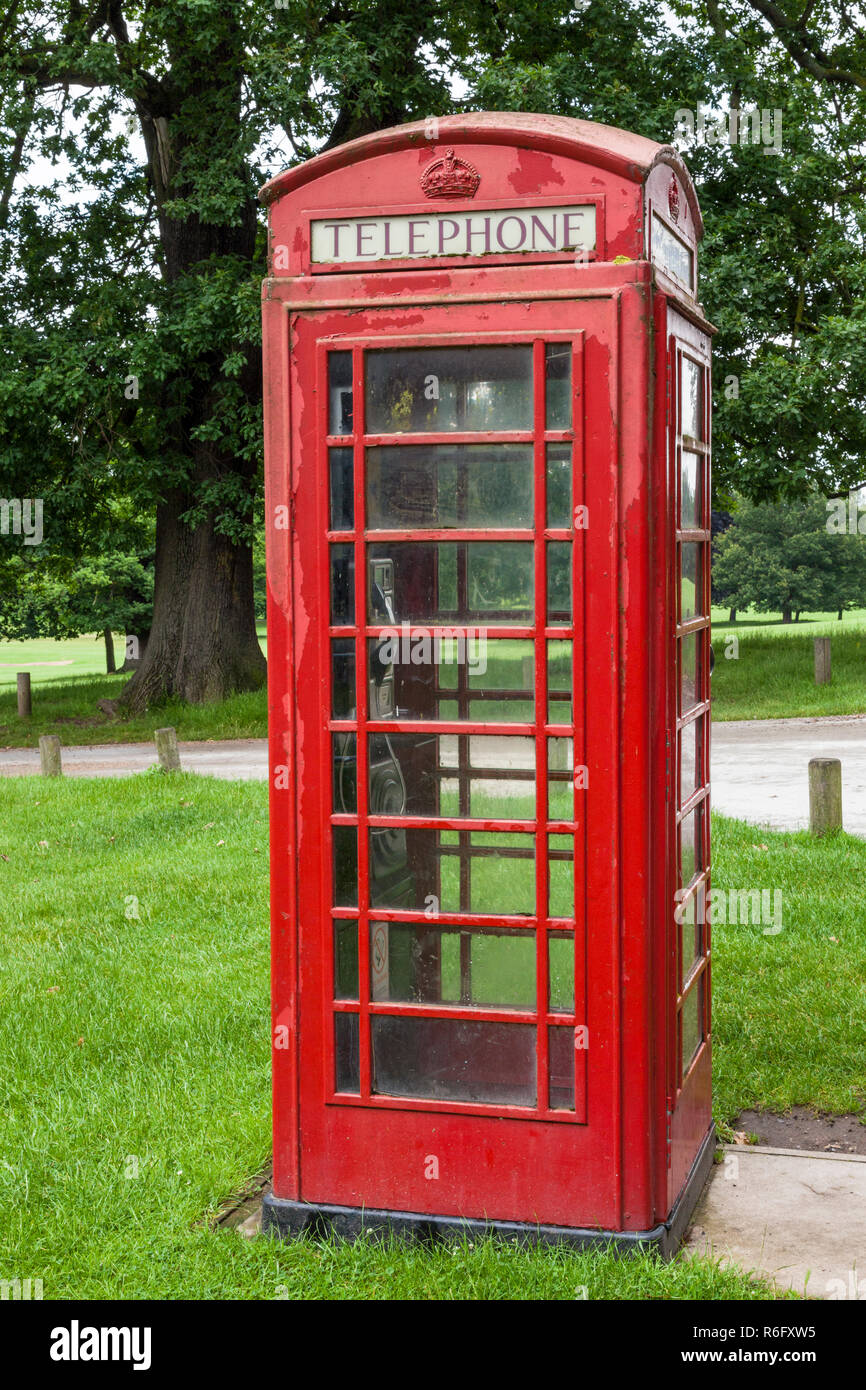 Old red telephone box surrounded by grass and trees at Wollaton Park ...