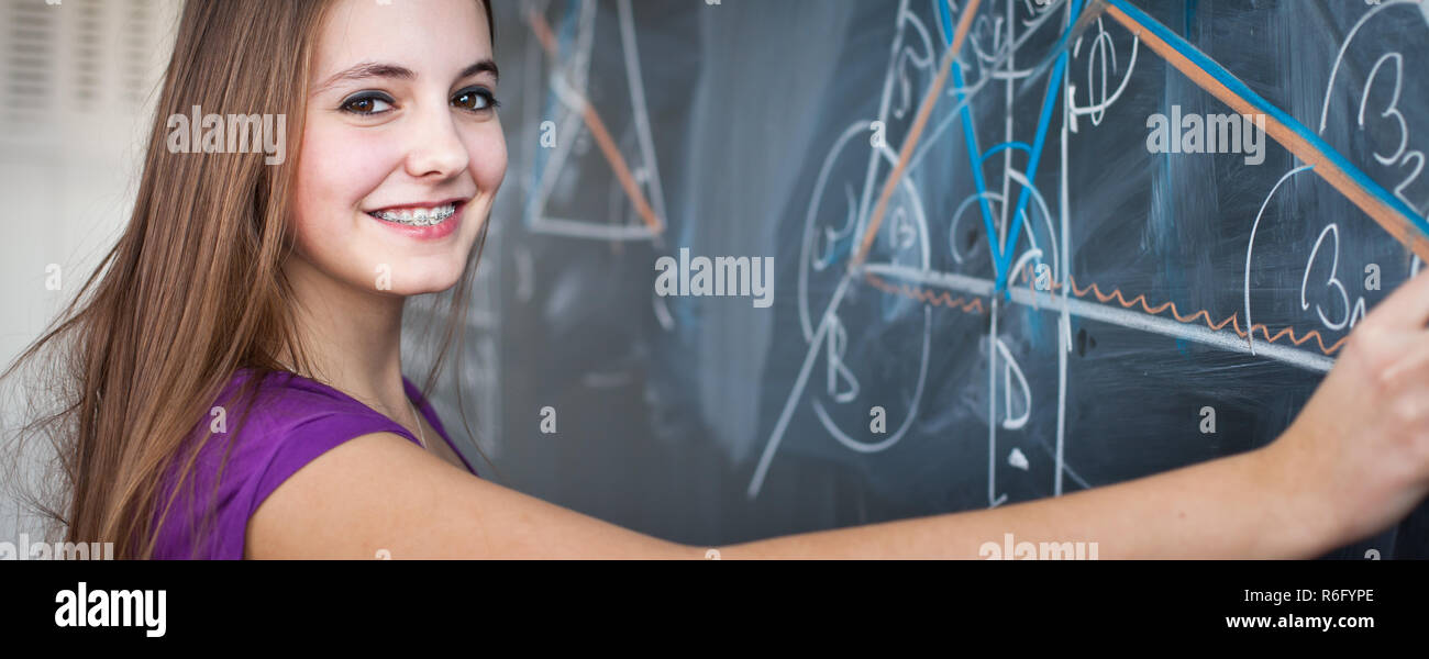 Portrait of a pretty young college student writing on the blackboard ...